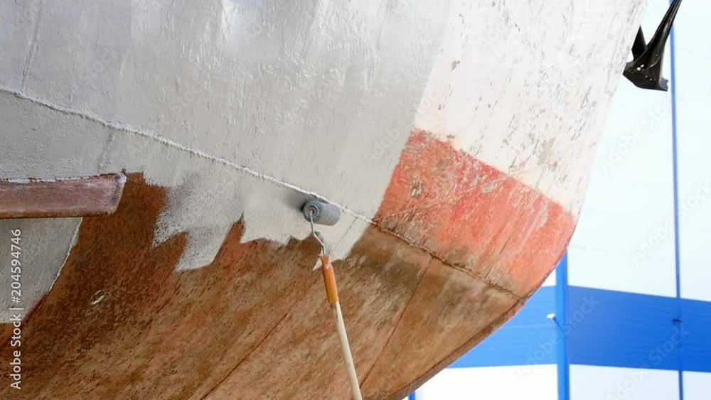 Worker paints metal of old rusty ship propeller at shipyard in port ...