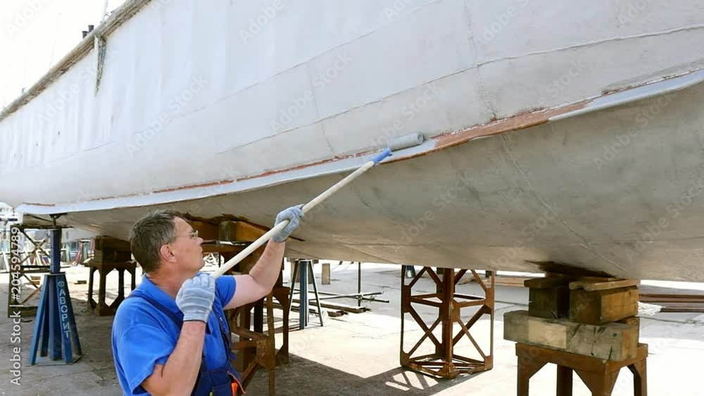 Worker paints metal of old rusty ship propeller at shipyard in port ...
