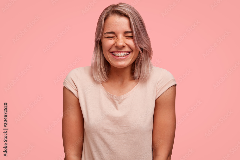 Positive European female laughs joyfully, listens funny joke, has broad ...