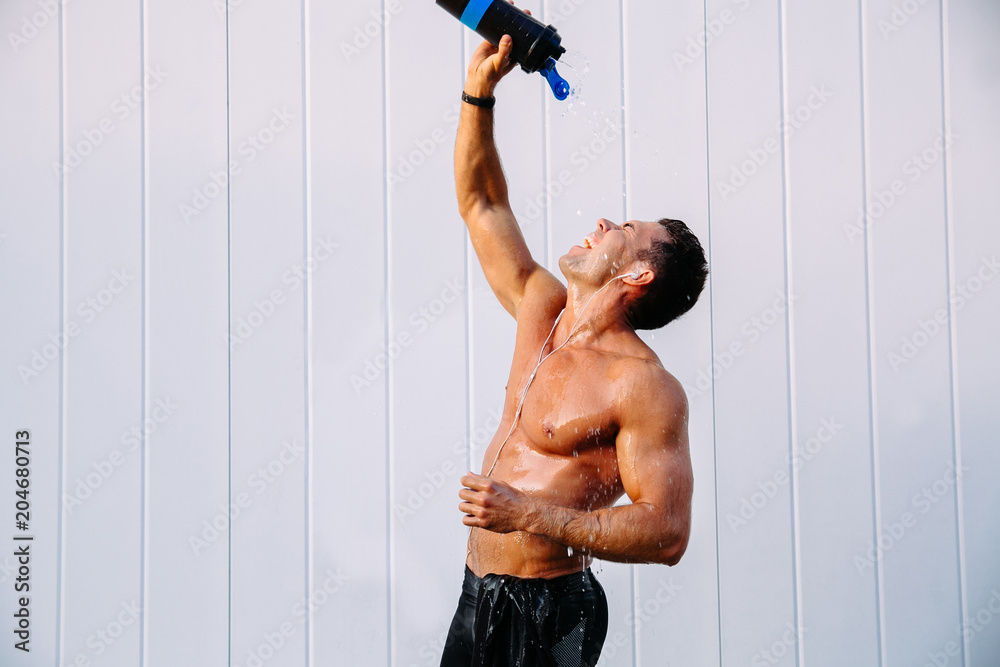 Side view of muscular man pouring out water from bottle on his body ...
