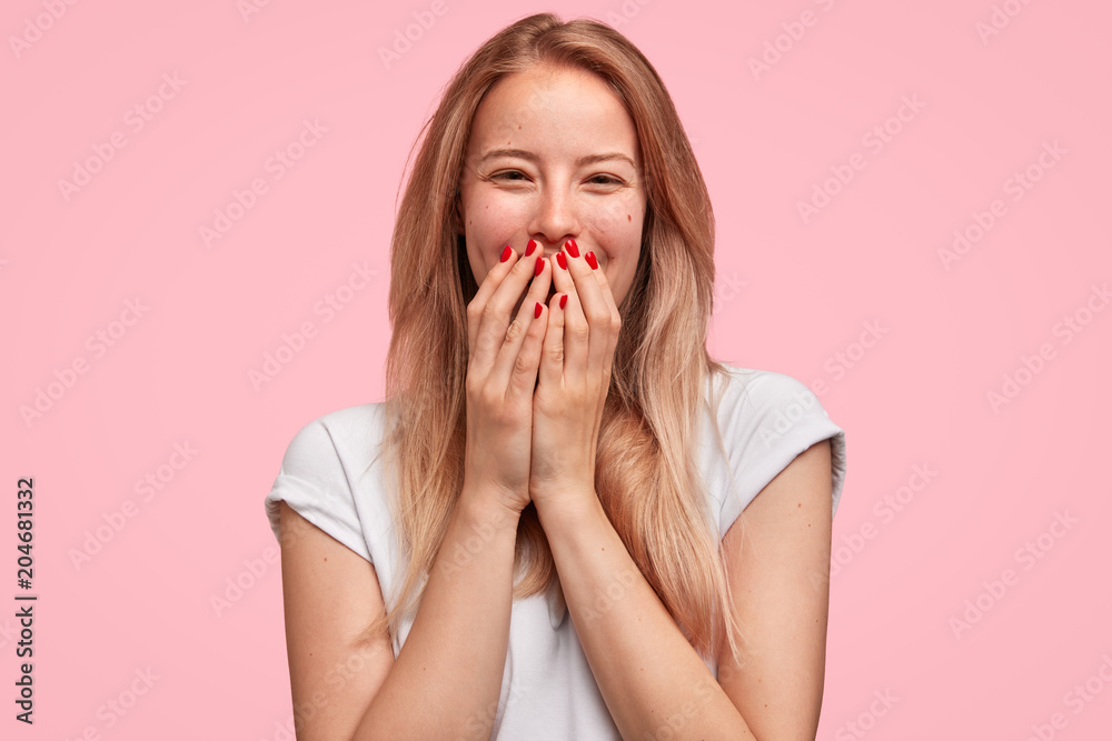 Horizontal shot of good looking young female giggles joyfully, covers ...