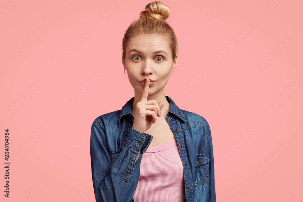 Pretty blonde female with no make up, makes silence sign, keeps fore ...