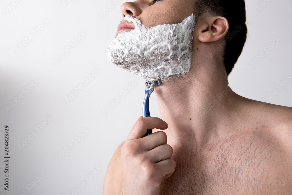 Low angle close up of chin of young man with foam is standing and ...