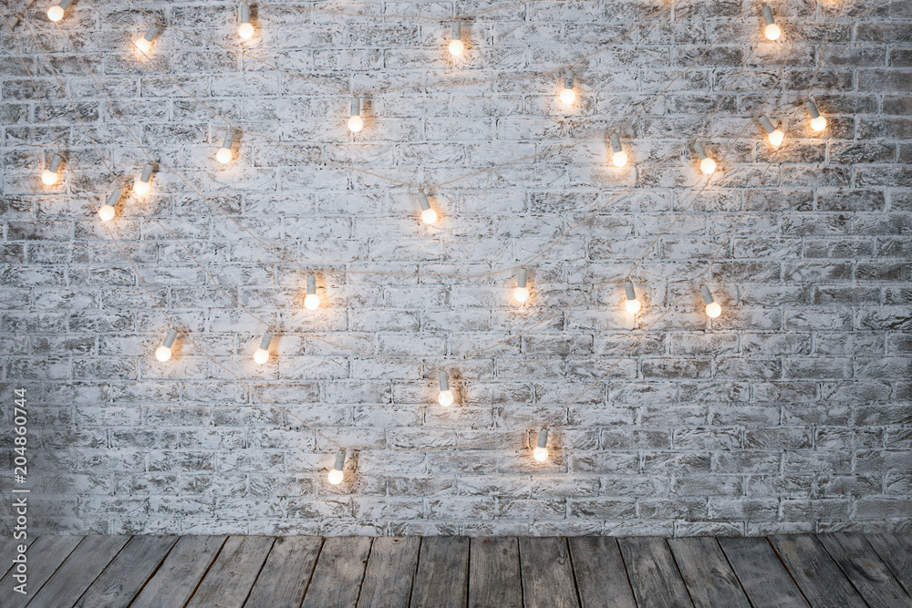 Light bulbs on white brick background with wooden floor. Vintage edison light bulbs garland in ...