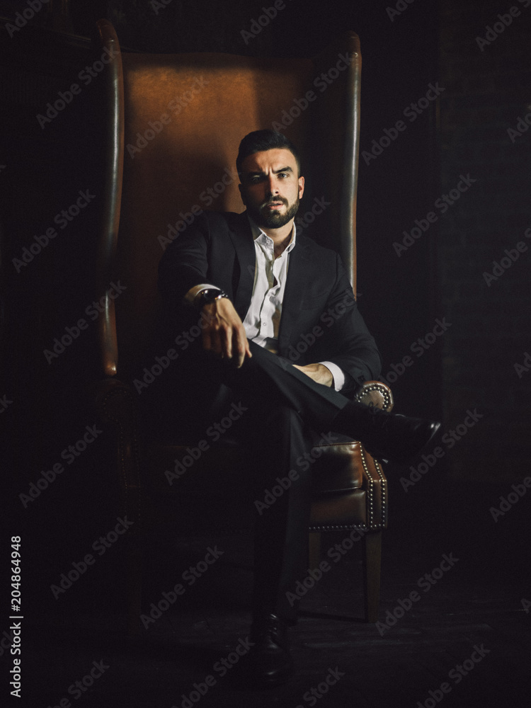 A handsome man with a beard and in a classic suit sits in a leather ...