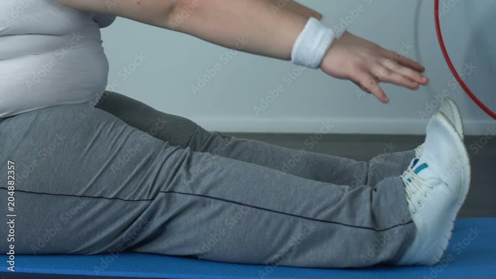 Fat belly person stretching legs sitting mat, trying to reach toes ...