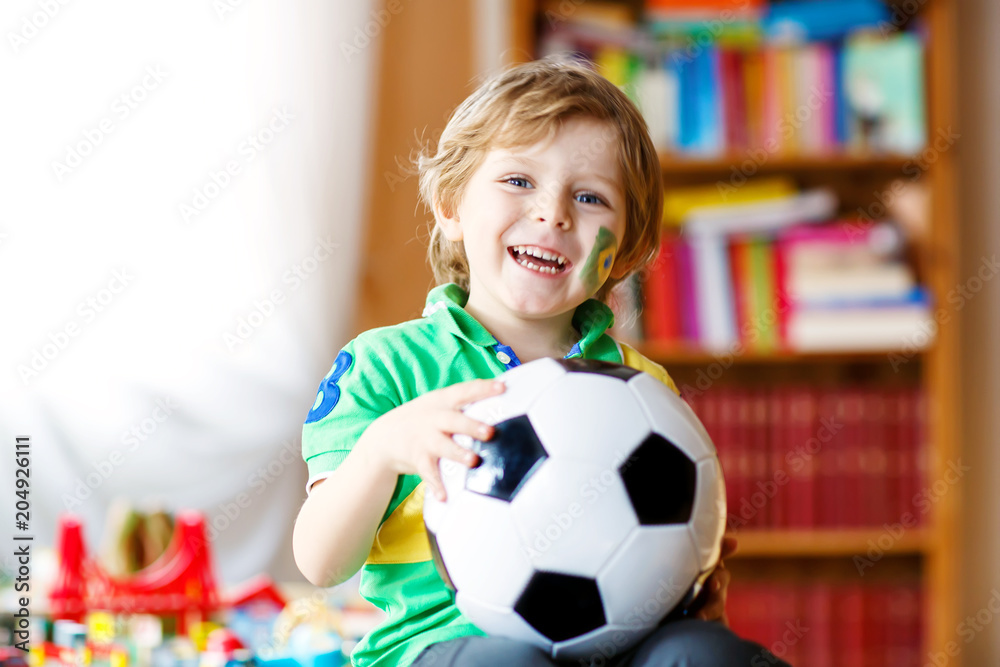 Little blond preschool kid boy with ball watching soccer football cup ...