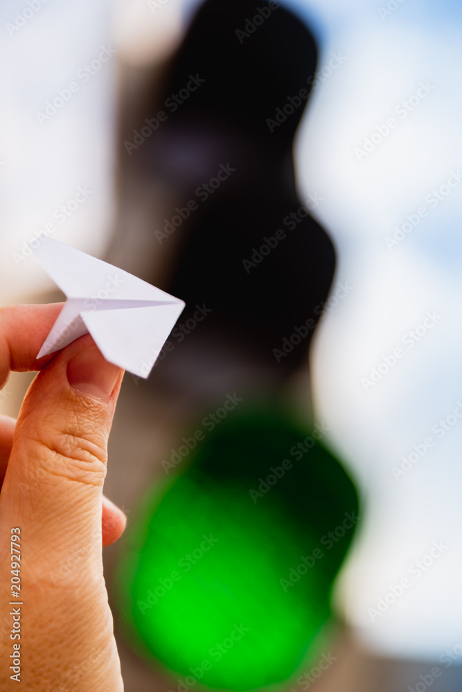One small paper airplane in hand against a traffic light background ...