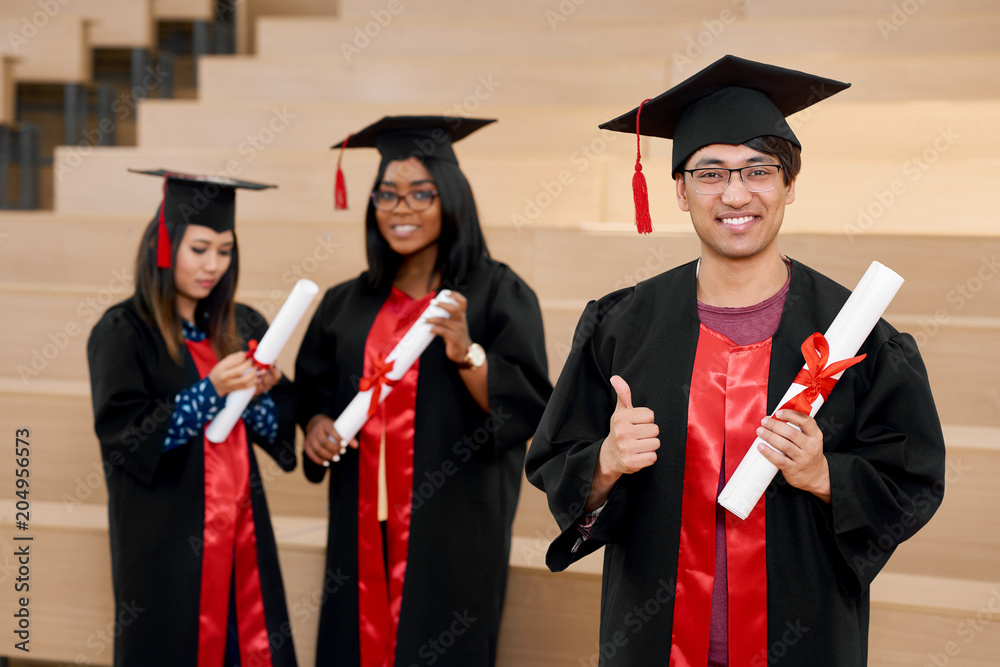 Smiling different nationalities graduates holding diplomas standing in ...