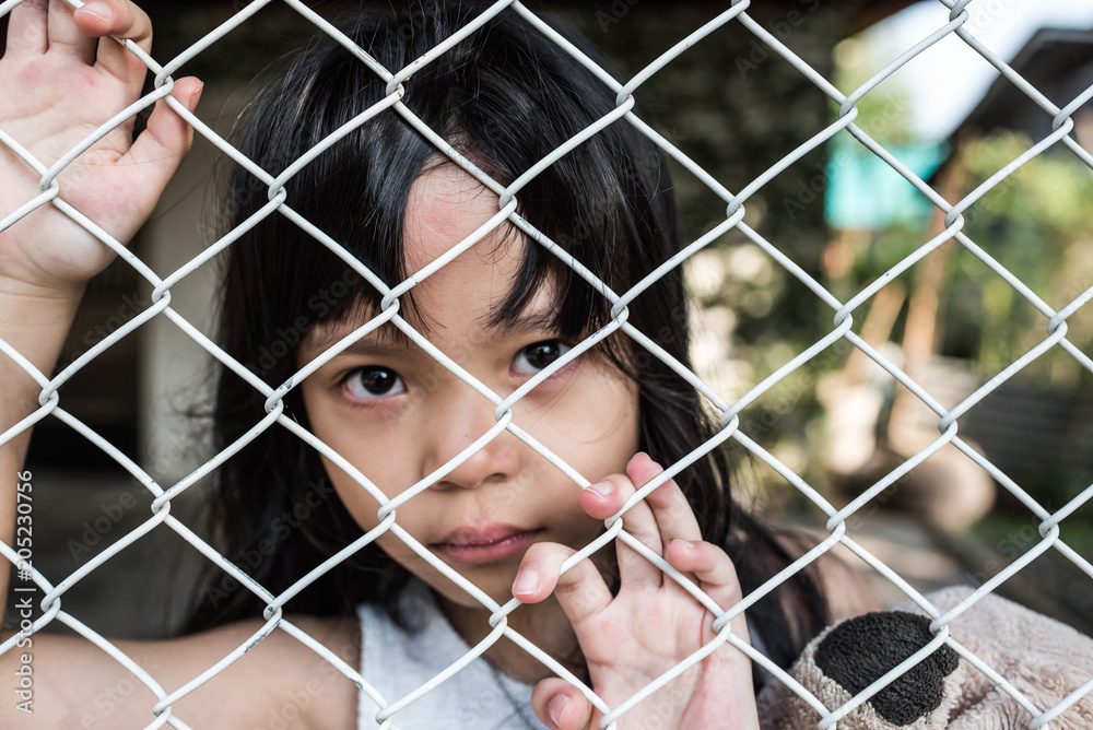 The sad Asian girl child, while sitting alone in cage was imprisoned ...