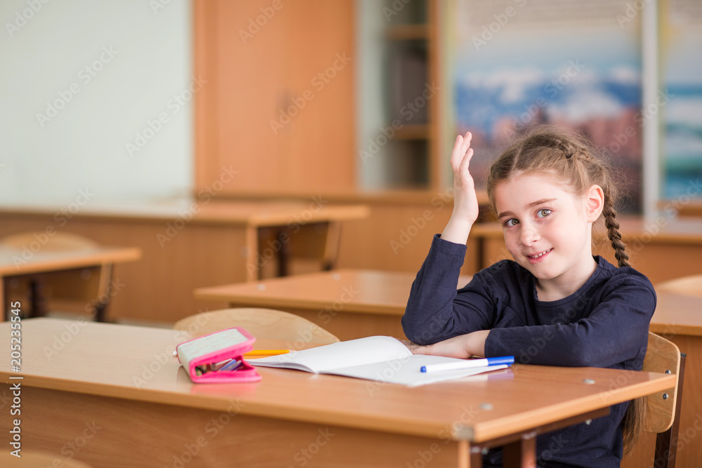 child girl sits at the Desk in the classroom, raises his hand and ...
