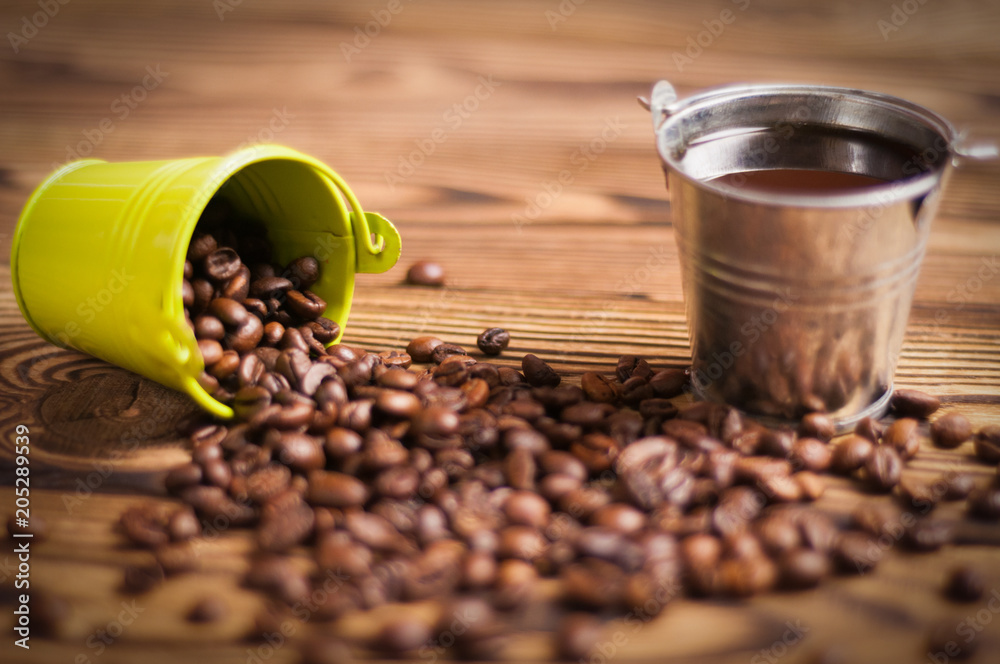 Full zinked bucket of black coffee near roasted beans poured out of ...