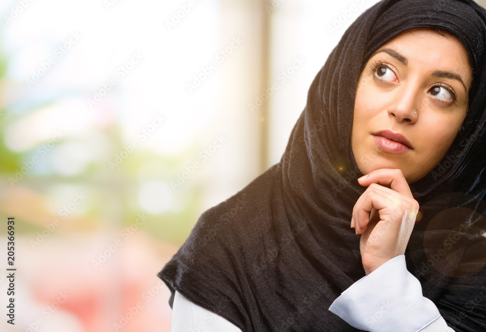 Young arab woman wearing hijab thinking and looking up expressing doubt ...