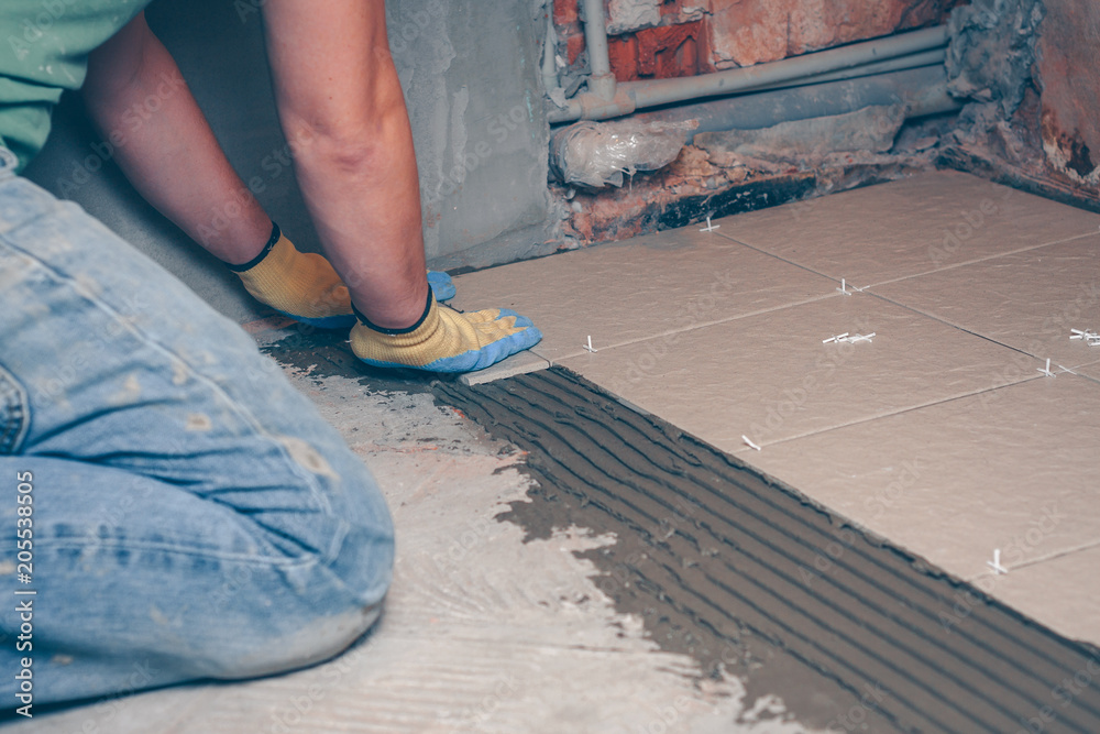 The worker carries out installation of a tile on a floor, finishing and ...