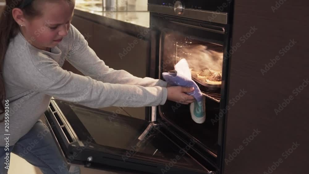 Girl opens oven and takes burnt cookies, smoke from overcooked food is ...