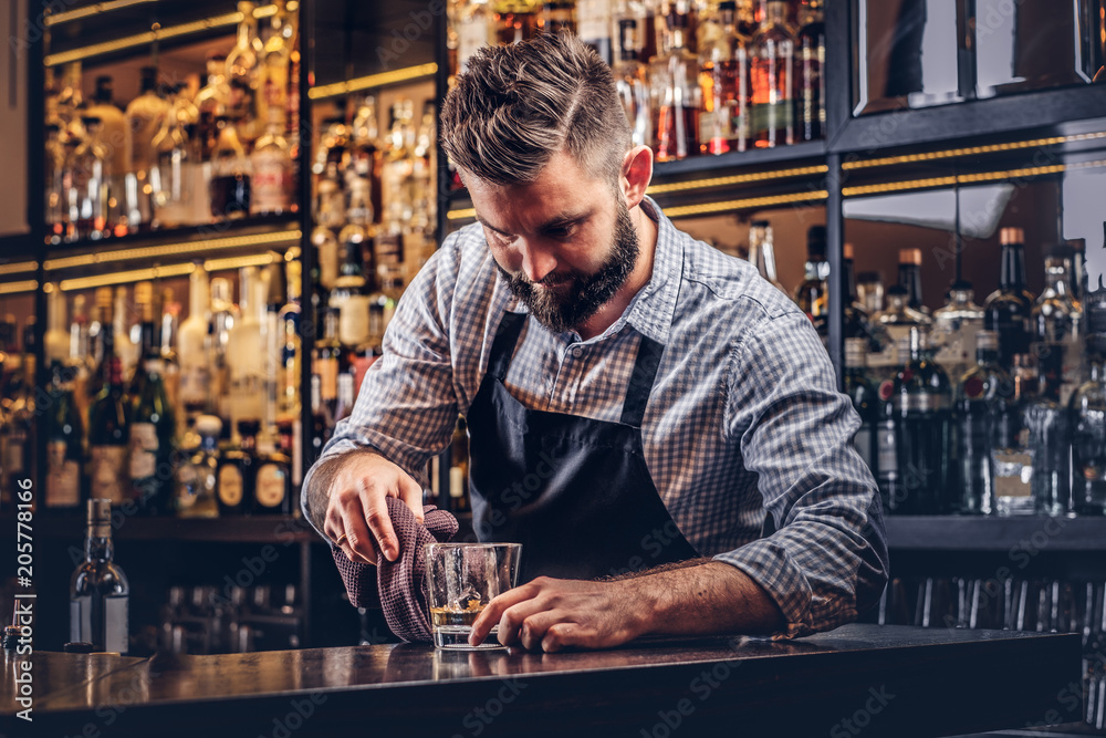 Stylish brutal barman in a shirt and apron makes a cocktail at bar ...