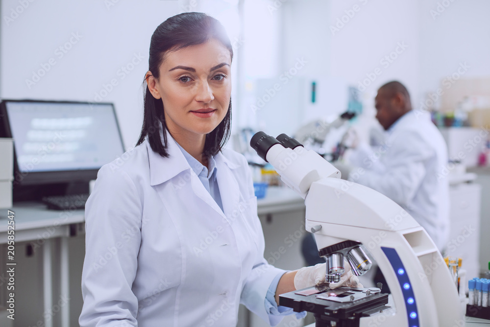 Feeling happy. Smiling smart scientist working with her microscope and ...