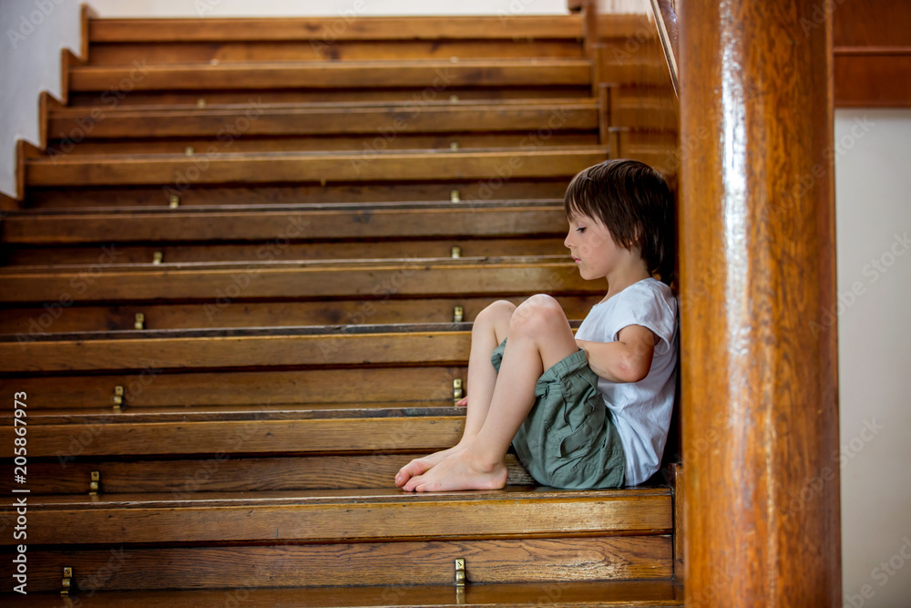 Sad child, sitting on a staircase in a big house, concept for bullying ...