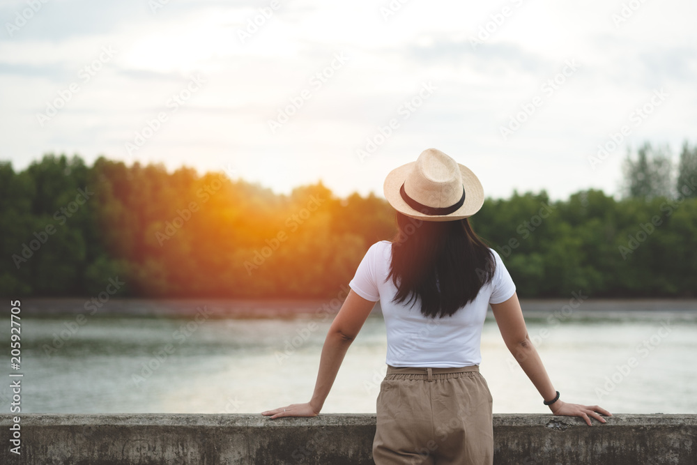 Back view of happy hipster woman in hat standing and looking at river ...