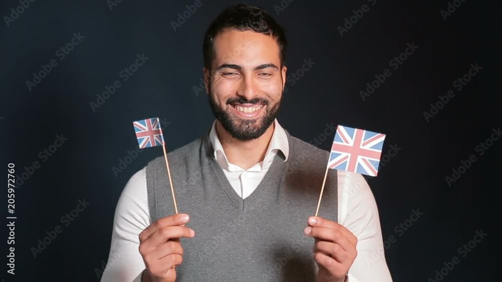 Smiling attractive man with black beard showing english flags happily ...