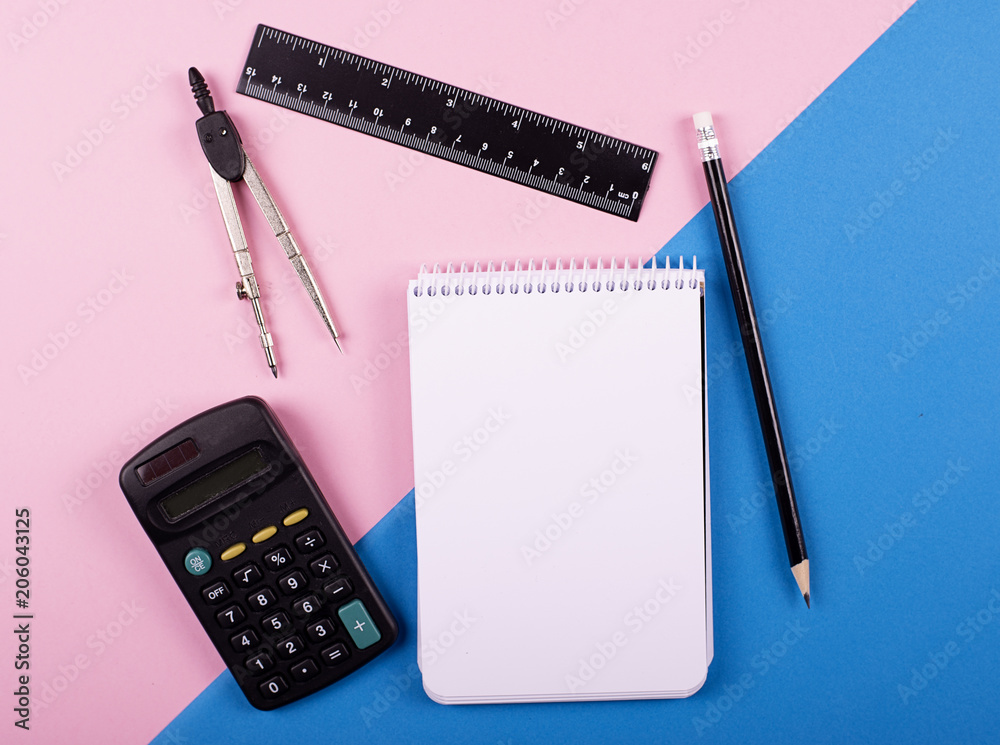 Notebook next to compass, calculator, ruler and pencil on blue and pink ...