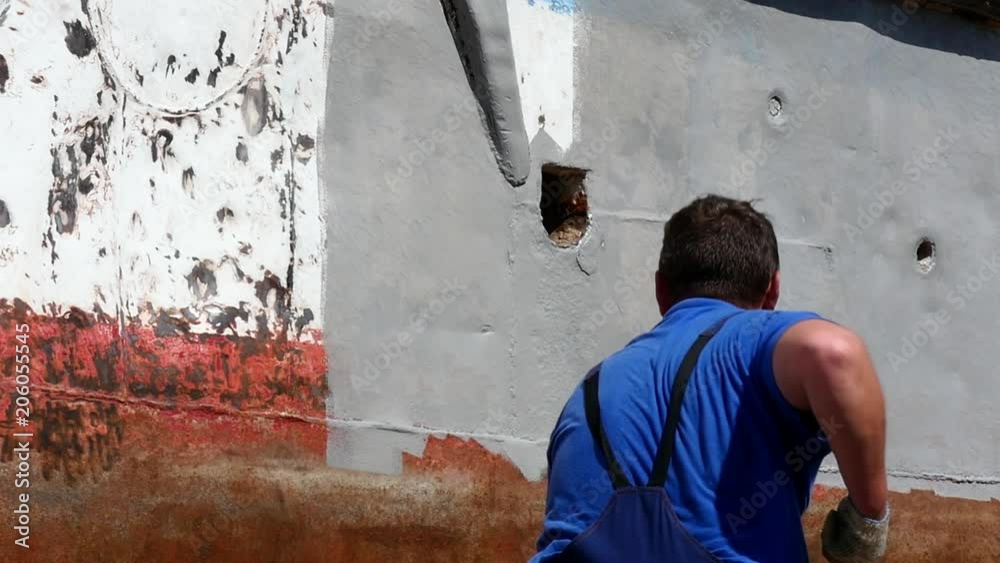 Worker paints metal of old rusty ship propeller at shipyard in port ...