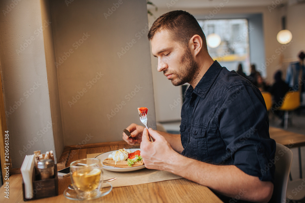 A picture of man sitting at the table and eating. He has a piece of ...