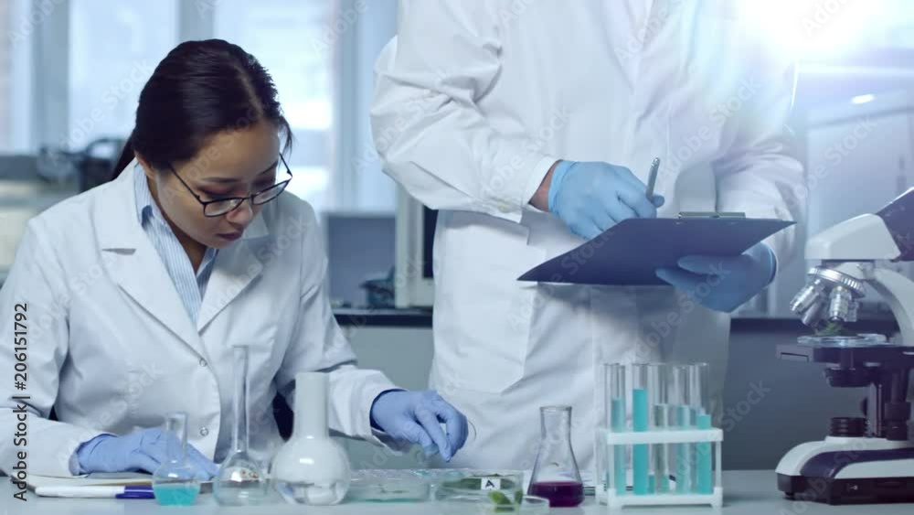 Tracking shot of three chemists working in laboratory, one using ...