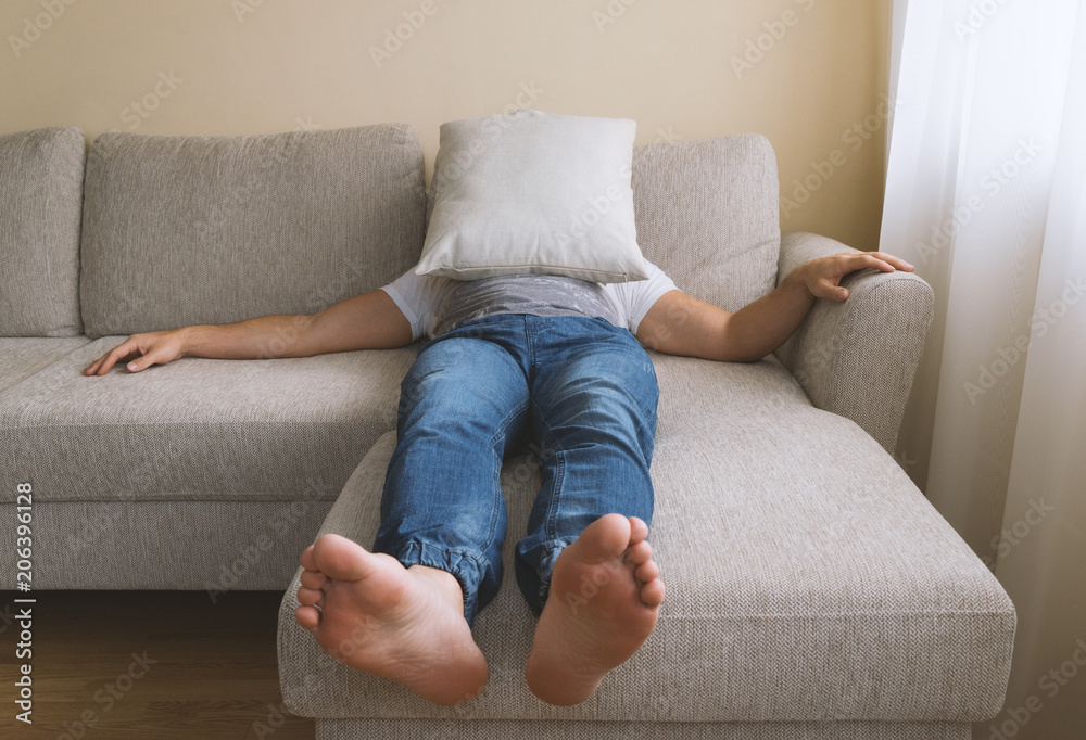 Faceless adult tired man in blue jogger jeans lying on beige sofa in ...