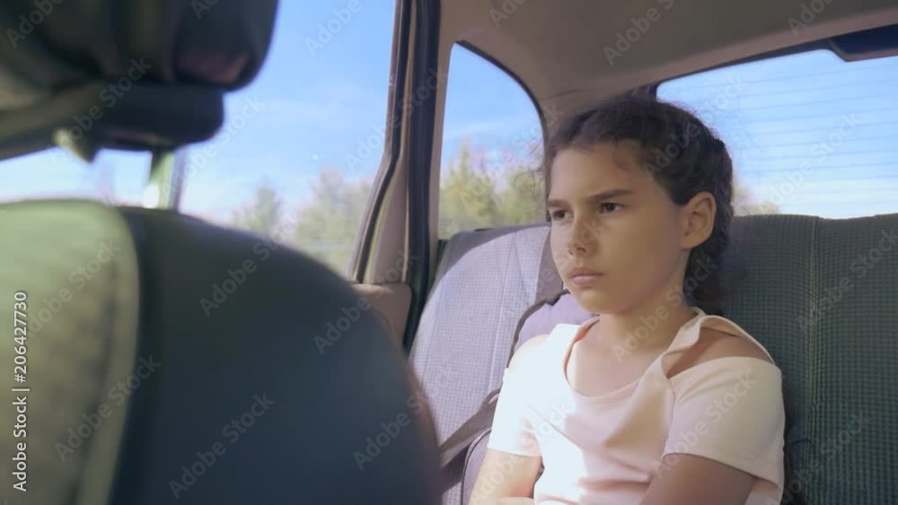 sad girl bored sitting in the car in the back seat travel. little girl ...