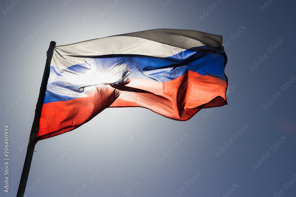 russian tricolor flag flying in slow motion and back lit by the sun ...