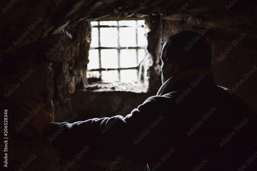 Man prisoner watching out from underground window, hands on the wall ...