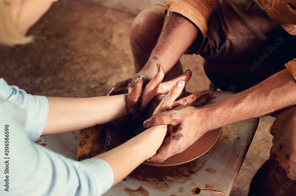 Hands of two people create pot on potter's wheel. Teaching pottery ...