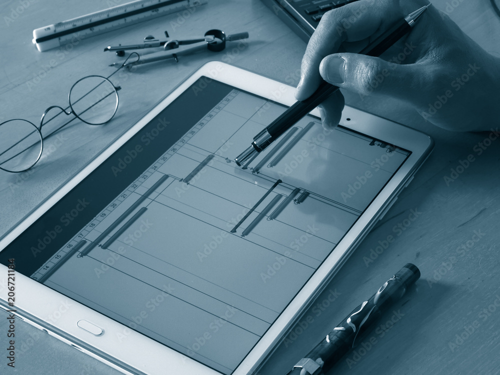 engineer working on tablet computer on chart of project time table ...