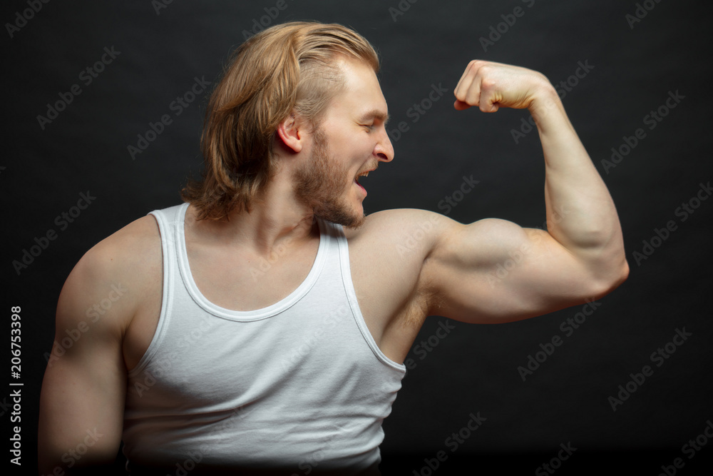 joyful athlete admiring with his strong arms isolated on the black ...