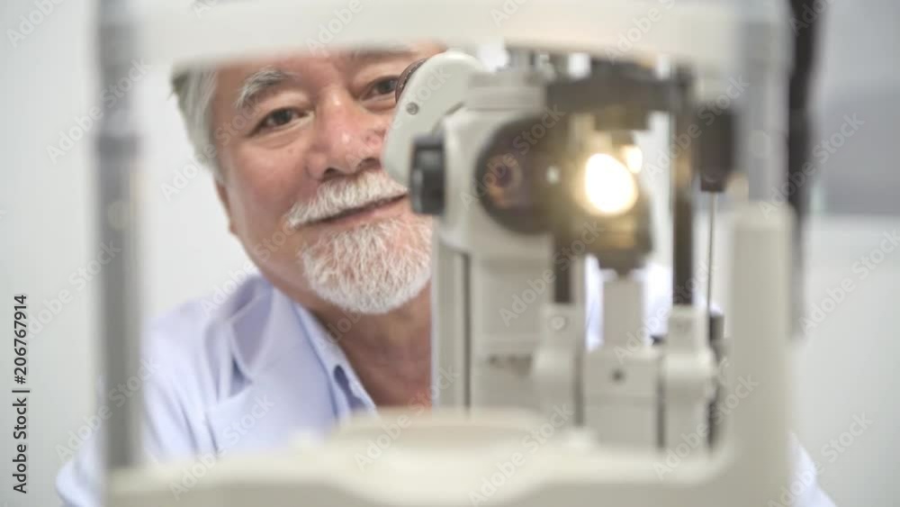 Optician at work in hospital. Senior chinese optician using eye scanner ...