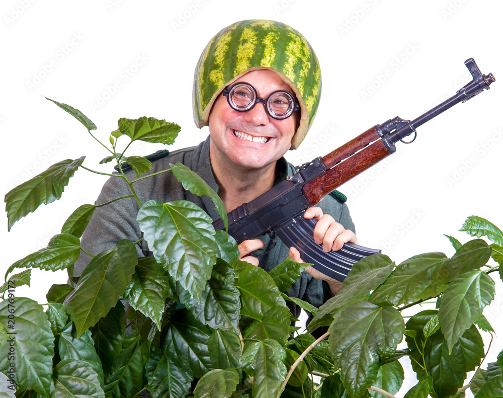 Funny cheerful soldier with a machine gun sticking out of the leaves ...
