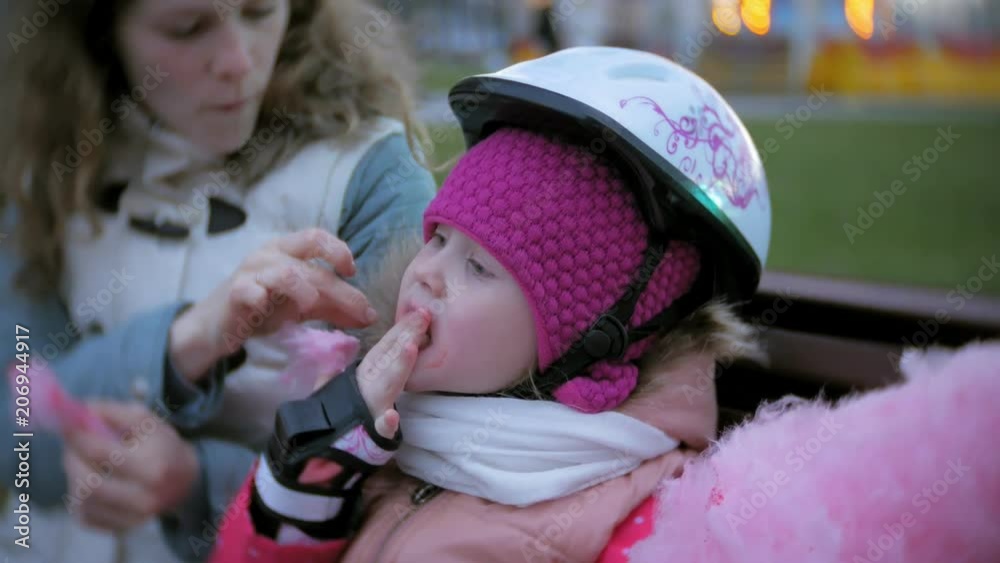 Beautiful little girl sitting on a bench in an amusement park, eating ...