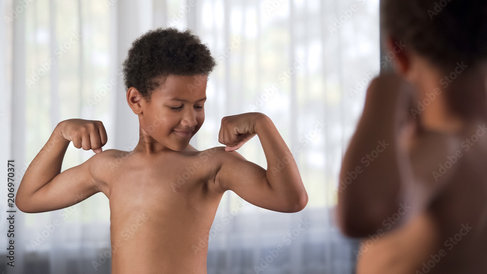 Cute african boy showing arm muscles in front mirror, sport power ...