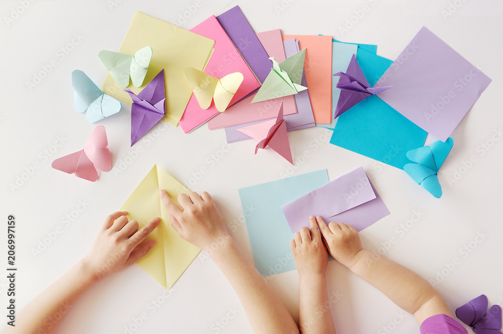 Children's hands do origami from colored paper on white background ...