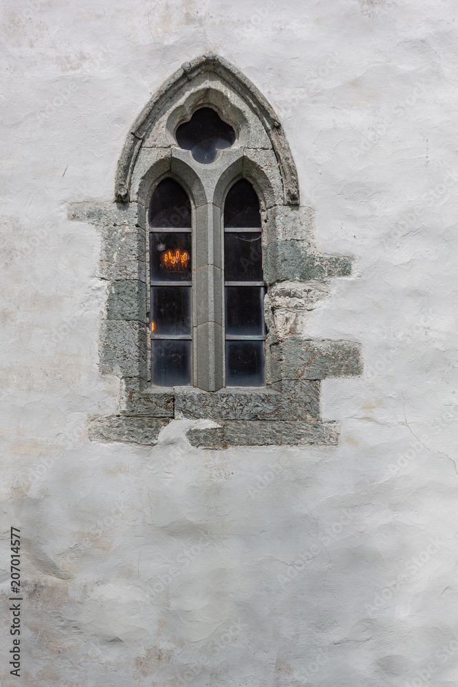 Old stained glass window on white stone wall of medieval stone church ...