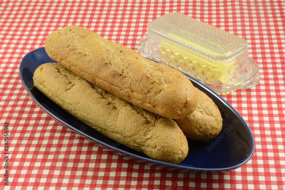 Whole wheat loaves of bread for submarine sandwiches on blue platter ...