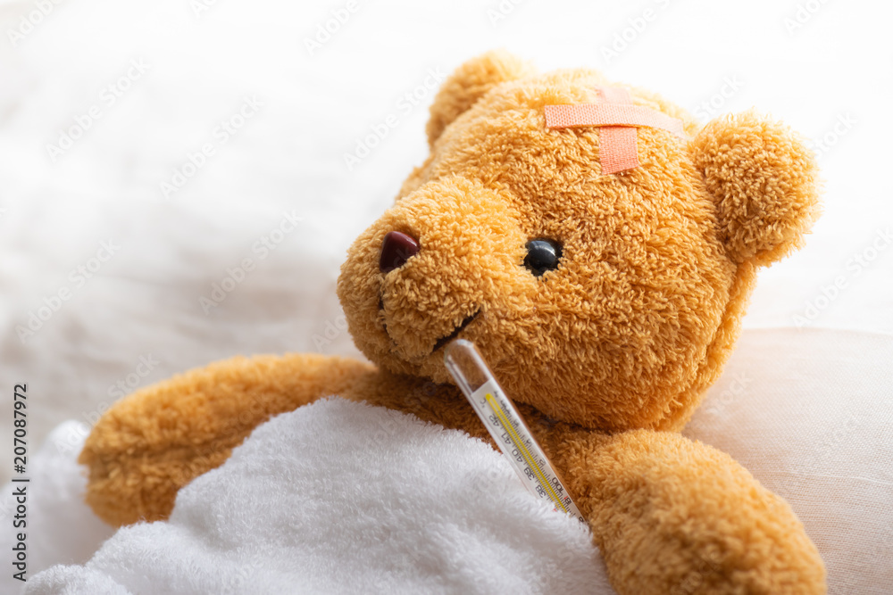 Teddy bear lying sick in hospital bed with with thermometer and plaster ...