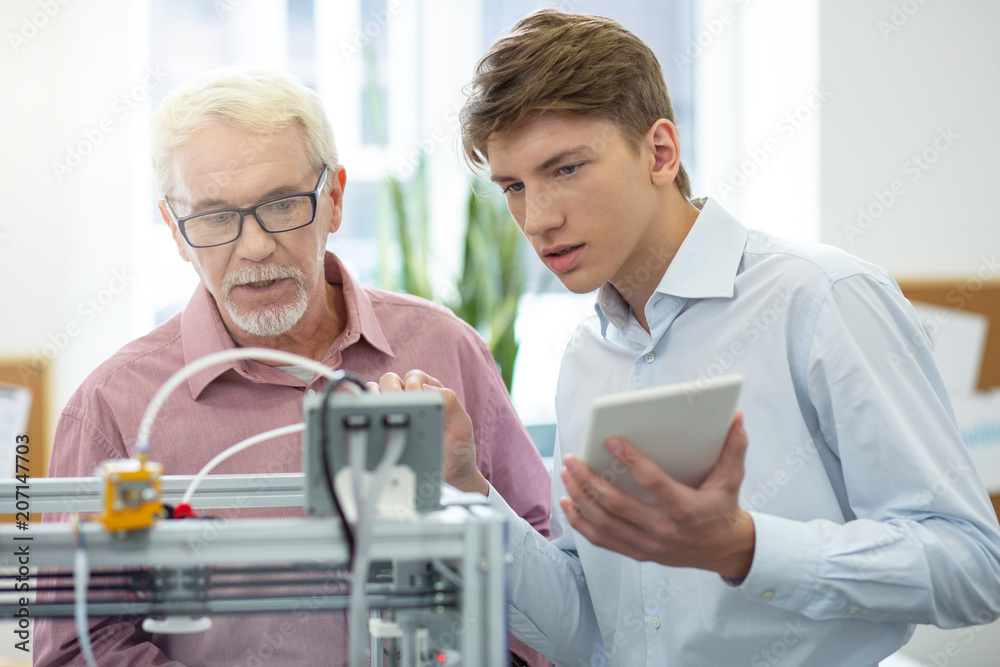 Constant support. Pleasant young man trying to run 3D printer while ...