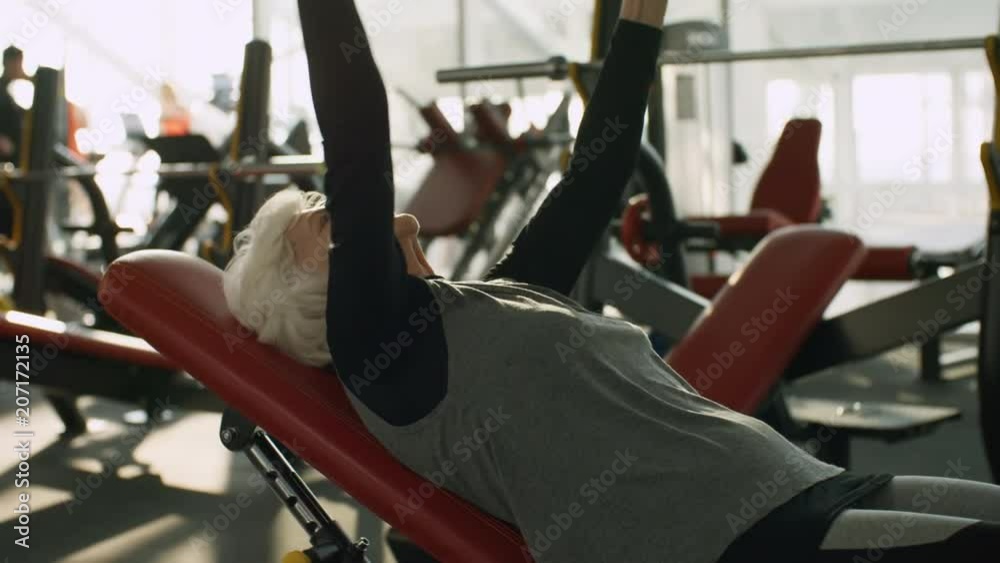 Vidéo Stock PAN of senior woman with grey hair training on bench gym ...