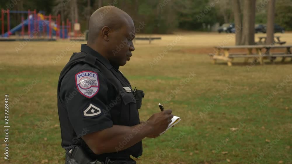 An African American police officer takes a notebook out of his uniform ...