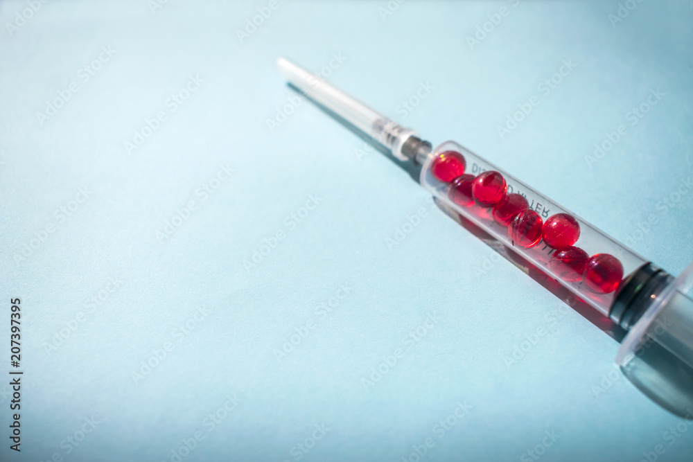 Red gel capsules inside a syringe with a needle on a blue background ...