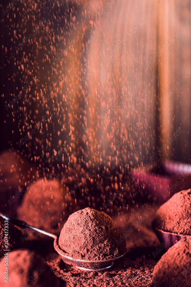 Chocolate truffles and falling cocoa powder on wooden background, macro ...