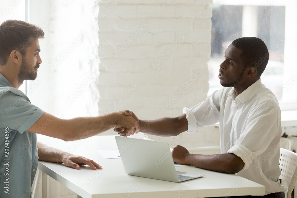 Serious African American boss shaking hand of Caucasian job candidate ...