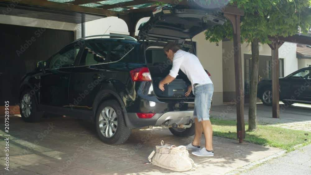 SLOW MOTION, LENS FLARE: Young man packing bags into a black car gets ...